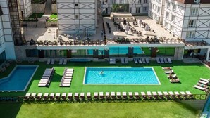 Pátio de hotel com duas piscinas, espreguiçadeiras e um pequeno jardim.