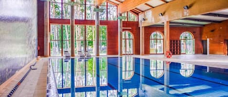 Piscina interior com reflexos nítidos, amplas janelas e vigas de madeira.