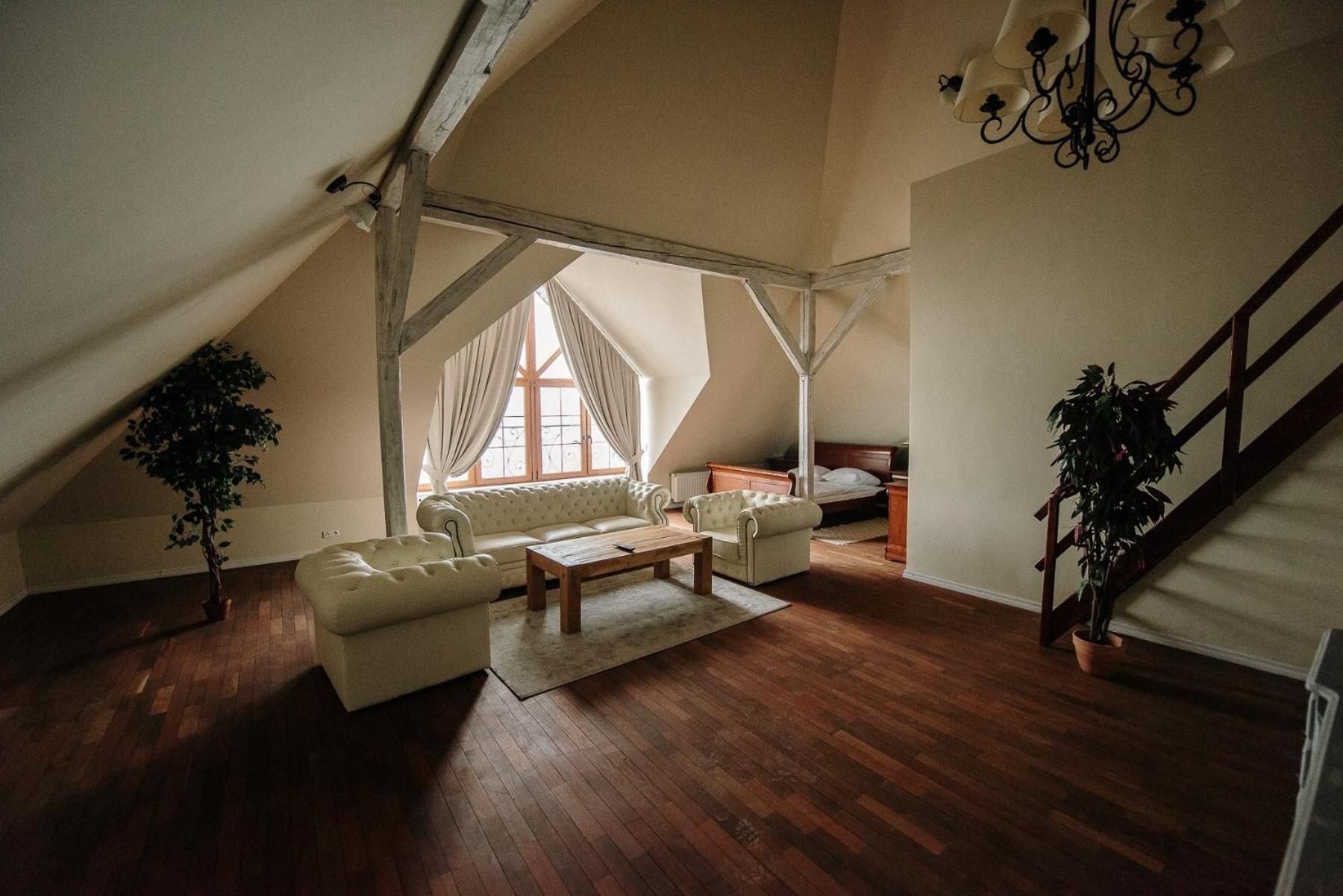 Quarto no sótão com teto inclinado, escada de madeira, um sofá, uma cama e um candelabro.