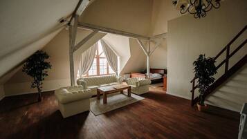 Quarto no sótão com teto inclinado, escada de madeira, um sofá, uma cama e um candelabro.