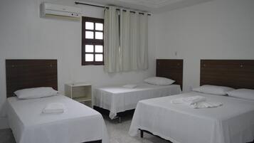 Quarto de hotel com duas camas de solteiro, uma pequena mesa de cabeceira e uma janela com cortinas.