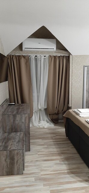 Quarto com teto inclinado, ar-condicionado embutido, um banco, uma mesa com papéis e uma cortina.