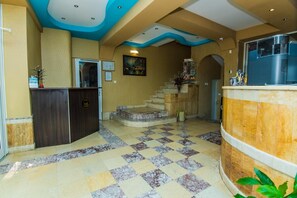 Um saguão de hotel com balcão de check-in, escada e mesa de recepção.