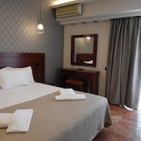 Quarto de hotel com uma cama grande, mesa de cabeceira de madeira, espelho e escrivaninha.