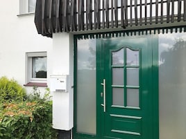 Uma porta verde com um painel de vidro, uma parede branca e uma janela com cortina branca.