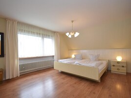 Quarto com cama, mesas de cabeceira, radiador e janela com cortinas.