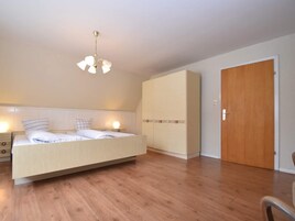 Quarto com cama, mesas de cabeceira, guarda-roupa e uma porta.