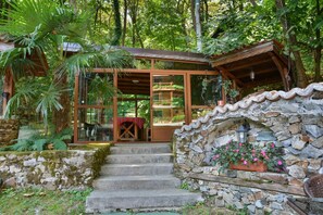 Estrutura de madeira rústica com parede de pedra e porta de vidro que dá para um espaço com toalha xadrez vermelha.