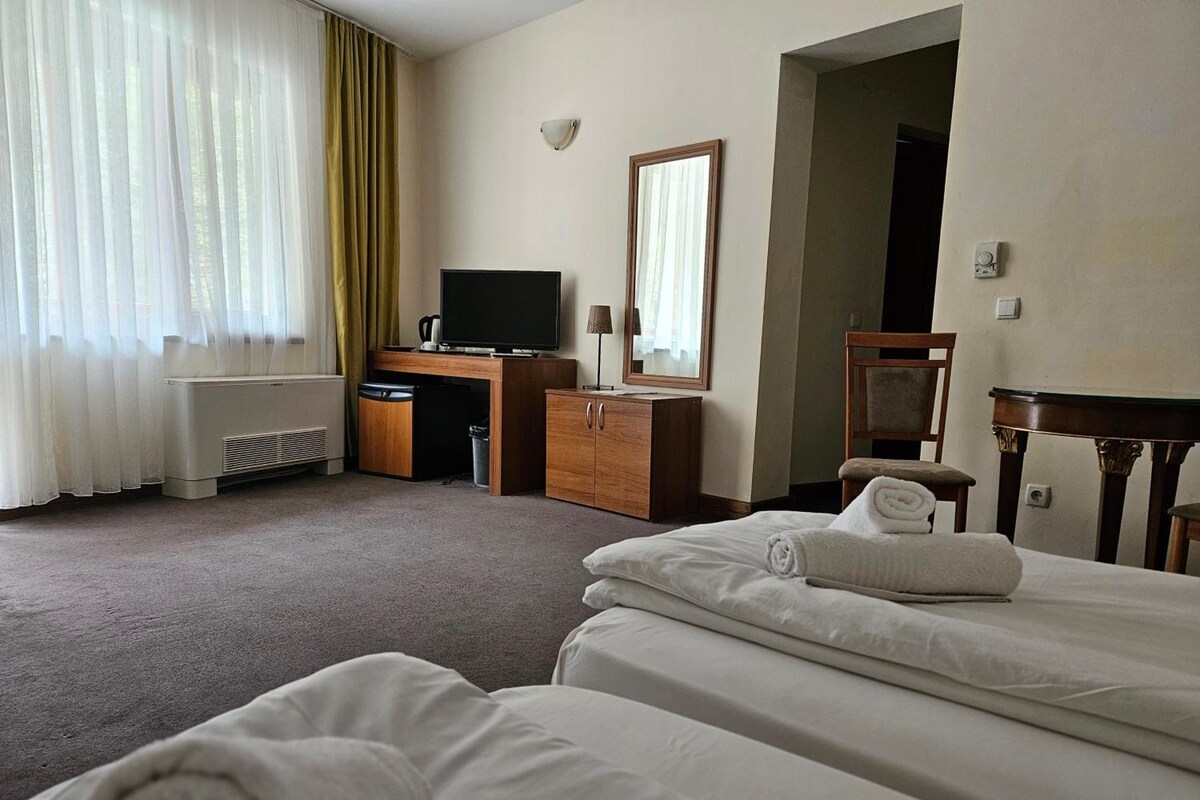 Quarto de hotel com duas camas, uma escrivaninha, televisão e um espelho.