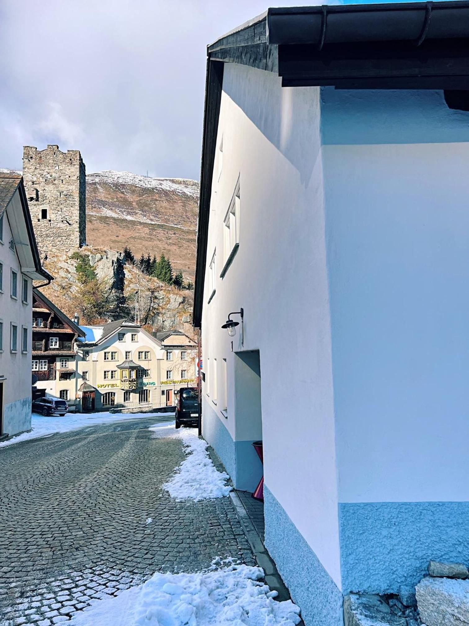 Uma rua de paralelepípedos com neve no chão, edifícios com arquitetura tradicional e um castelo ao fundo.
