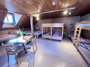 Um quarto de dormitório com beliches, uma escrivaninha, cadeiras e uma janela.