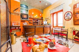 Uma área de refeições com um bar, uma televisão e diversos alimentos e bebidas sobre a mesa.