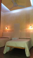 Quarto com duas camas, ventilador de teto e luminárias na parede.