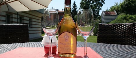 Uma garrafa de vinho Tokaji Aszali, dois copos de vinho e um tecido rosa sobre uma mesa ao ar livre.