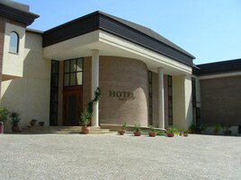 Entrada de hotel com uma ampla porta em arco, colunas e plantas em vasos.
