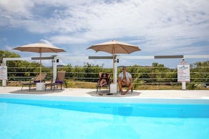 Uma área de piscina com espreguiçadeiras, guarda-sóis e uma placa com as regras da piscina.