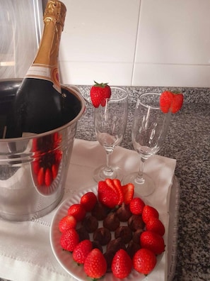 Uma garrafa de champanhe, dois copos e um prato de morangos e chocolate.