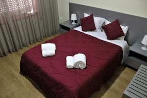 Quarto de hotel com uma cama grande, duas almofadas, mesa de cabeceira com abajur e janela com cortinas.