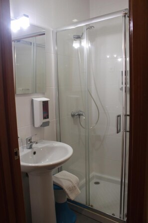 Casa de banho moderna com cabine de chuveiro de vidro, lavatório branco e espelho.