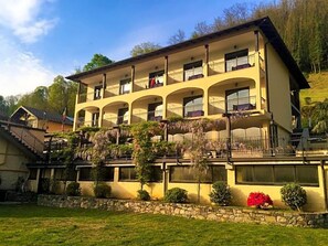 Um hotel com vários andares, varandas, fachada de pedra e um jardim ajardinado.