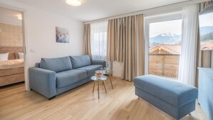Sala de estar moderna com sofá, uma mesinha com copos e uma garrafa de água, e vista para uma montanha através de amplas janelas.