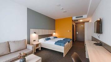 Quarto de hotel com cama, escrivaninha, cadeira, sofá e televisão.