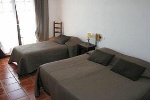 Duas camas de solteiro com cabeceiras, uma mesa de cabeceira com abajur e uma cadeira.