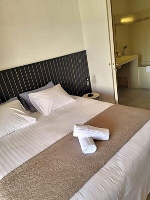 Quarto de hotel com cama, mesa de cabeceira e banheiro visível por uma porta aberta.