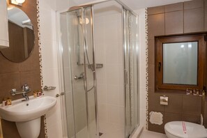 Casa de banho com chuveiro em cabine de vidro, lavatório com artigos de higiene e sanita com toalha.