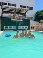 Piscina com estrutura de telhado de palha e placa indicando 'nacho hostel' ao fundo.