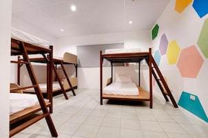 Quarto com beliches, paredes brancas e um vibrante ornamento hexagonal na parede.