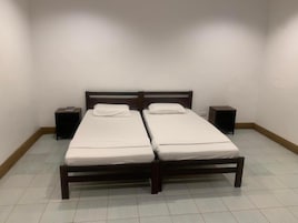 Quarto com duas camas de solteiro, mesa de cabeceira em cada lado e piso em azulejos.