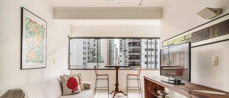 Uma sala de estar moderna com sofá, mesa de jantar com cadeiras, televisão e uma janela grande com vista para a cidade.