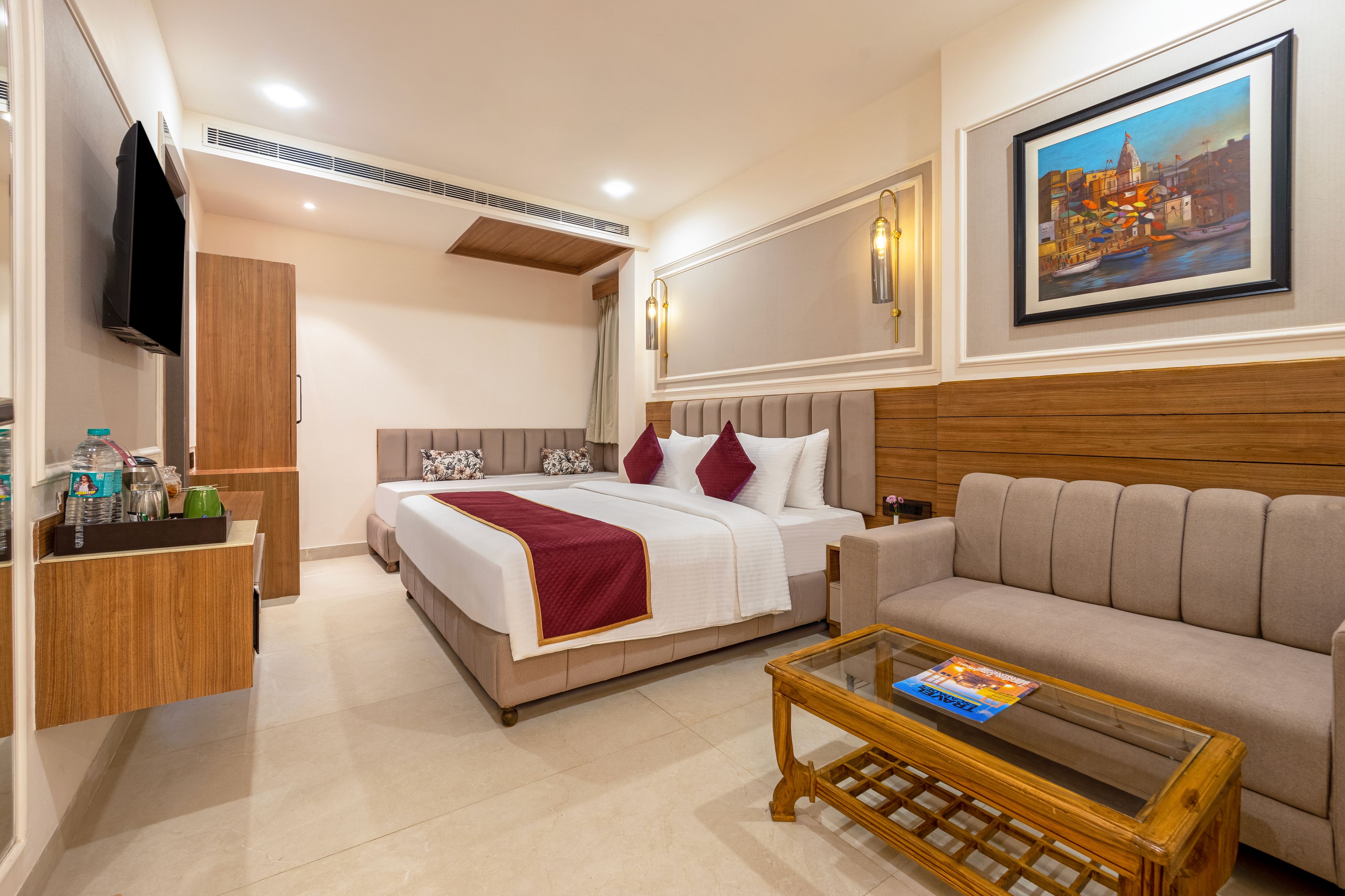 Quarto de hotel com cama, sofá, mesa de centro, televisão e um quadro na parede.