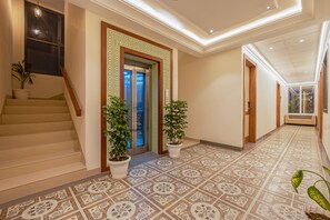 Corredor com piso estampado, escada e duas plantas em vasos.