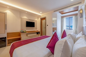 Quarto de hotel com uma cama grande, televisão de tela plana na parede, mesa de cabeceira e uma janela com cortinas.