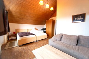 Quarto com cama, sofá, teto de madeira e um quadro na parede.