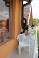 Varanda com uma cadeira de plástico branca, grade de metal e janela com vista para uma área residencial.