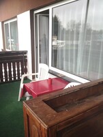 Quarto com uma janela grande, um banco de madeira, uma mesa vermelha e uma cadeira branca.