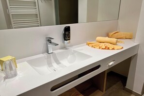 Casa de banho moderna com lavatório branco, dispensador de sabonete líquido e toalhas dobradas com cuidado.
