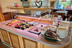 Balcão de buffet com diversos alimentos e utensílios de servir.