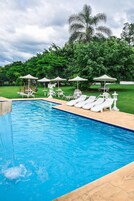 Piscina com espreguiçadeiras e guarda-sóis, cercada por vegetação.