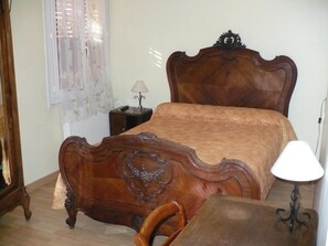 Quarto com cama de madeira, mesa de cabeceira, luminária e cadeira.