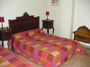 Quarto com cama de madeira, duas mesas de cabeceira, uma cadeira e colcha acolchoada.