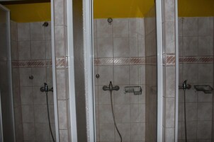Três boxes de chuveiro lado a lado, com paredes azulejadas e uma parede de destaque amarela.