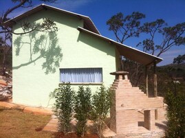 Um edifício térreo com fachada verde clara, uma janela com cortina e uma escadaria de pedra que leva a um alpendre.