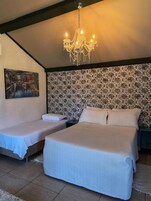 Quarto com duas camas de solteiro, uma cama grande, um lustre, papel de parede estampado e um quadro na parede.