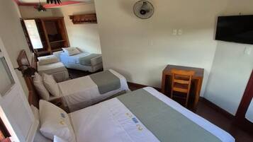 Quarto de hotel com duas camas, uma escrivaninha, uma cadeira, um ventilador e ventoinha no teto.