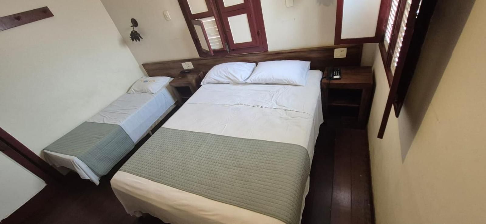 Quarto de hotel padrão com duas camas, uma mesinha de cabeceira e uma pequena mesa.