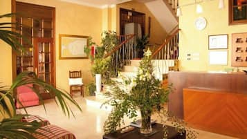Um saguão de hotel com balcão de recepção, escada e área de estar com mesa de centro e cadeiras.